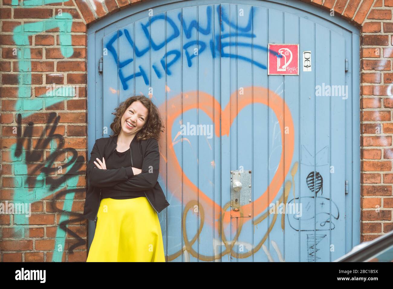 Portrait of a happy brunette woman standing in front of a brick wall ...