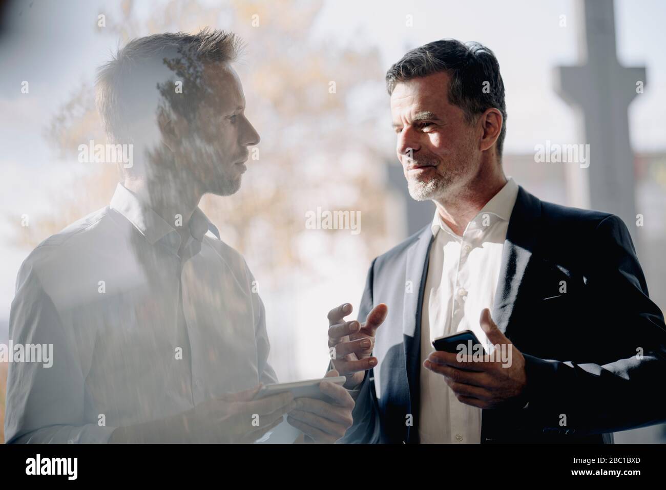 Two businessmen talking at the window Stock Photo - Alamy