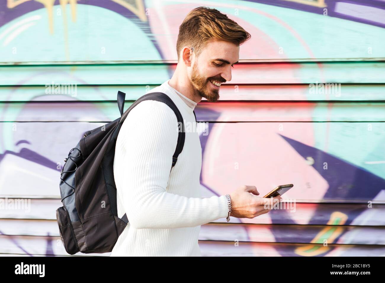 Smiling man at a graffiti wall using cell phone Stock Photo - Alamy