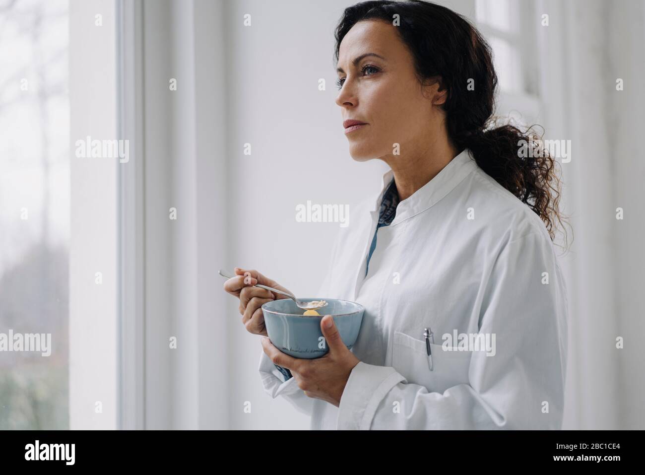 Female doctor eating a snack, standing at window Stock Photo - Alamy