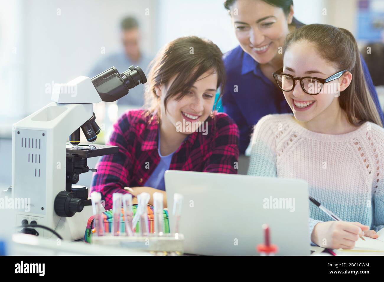 Female teacher and girl students using microscope and laptop ...