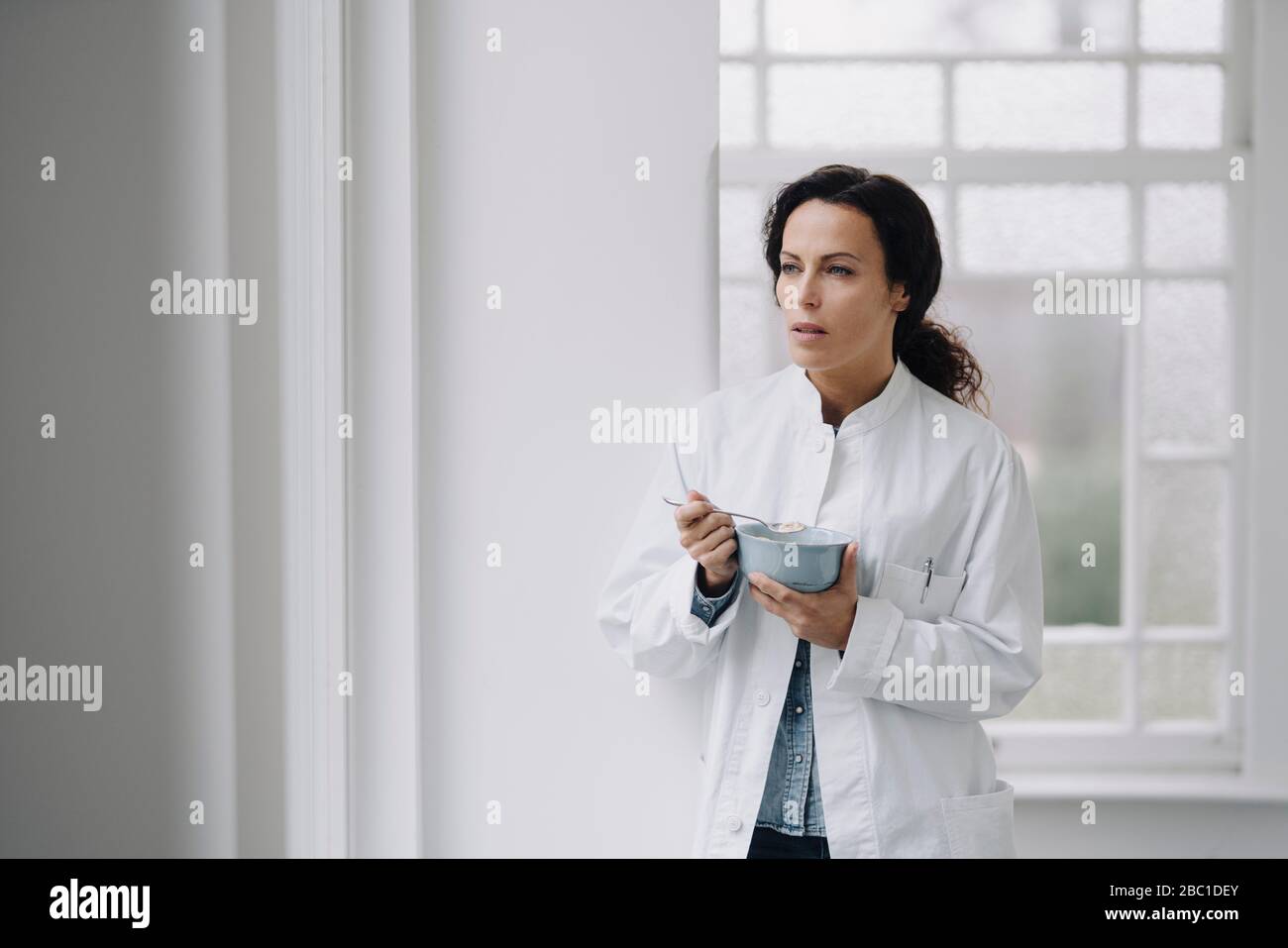 Female doctor eating a snack, standing at window Stock Photo - Alamy