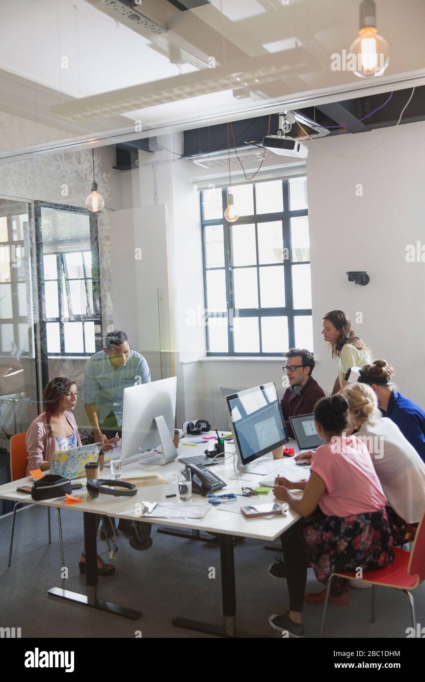 Designers meeting, working at computers and laptops in open plan office ...