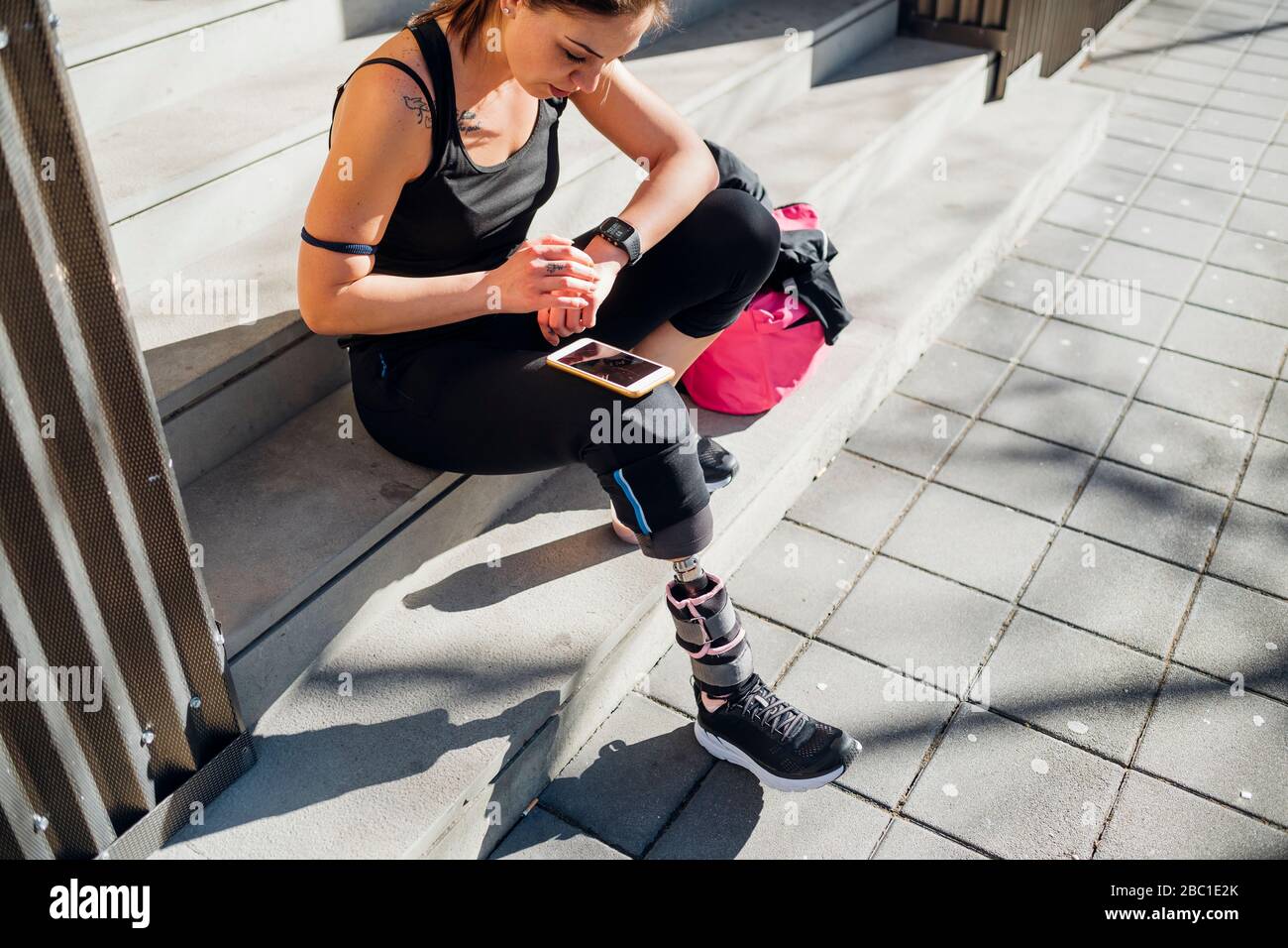 Sporty young woman with leg prosthesis sitting on stairs in the city ...