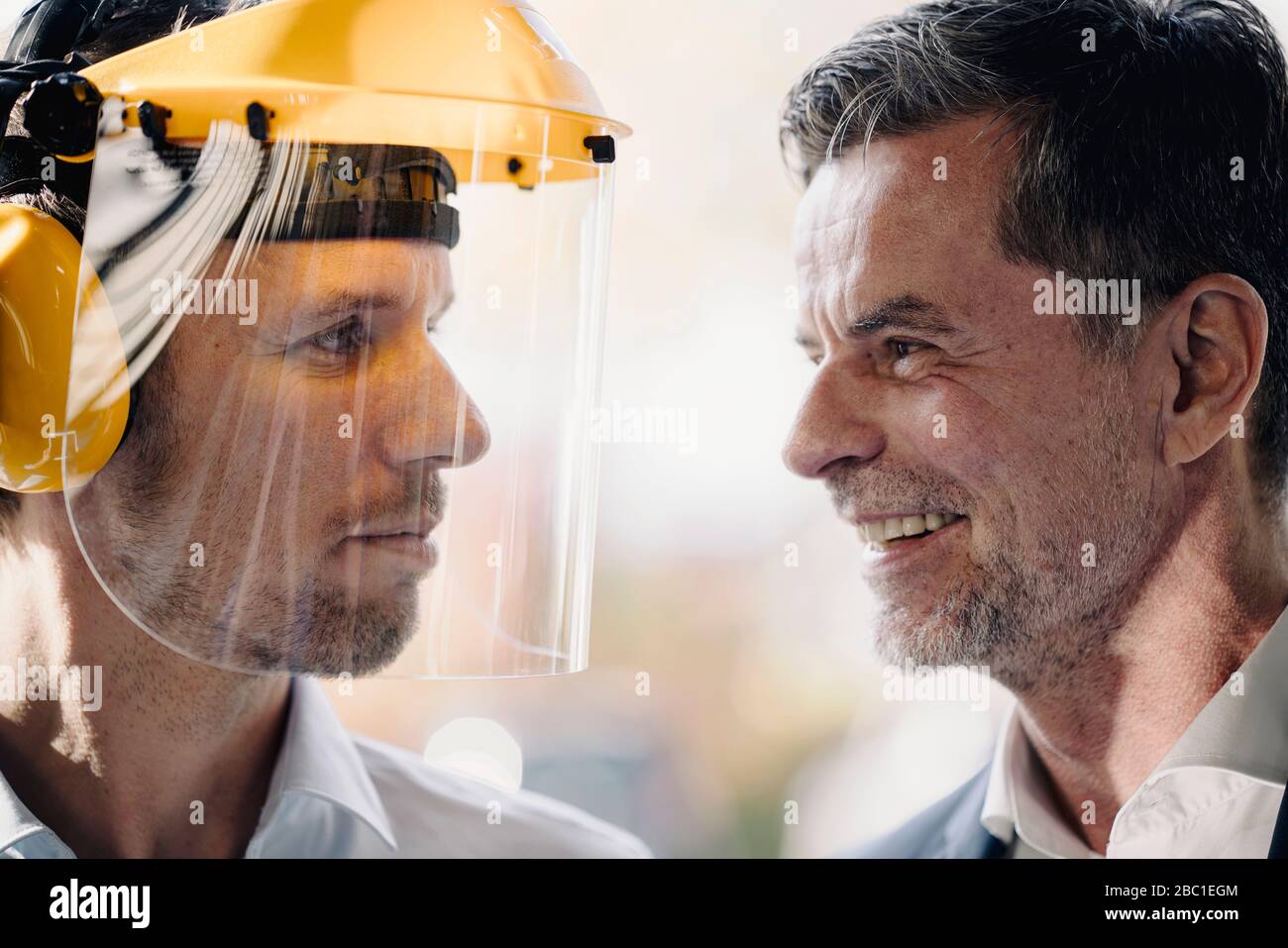 Smiling businessman and man wearing safety helmet facing each other ...