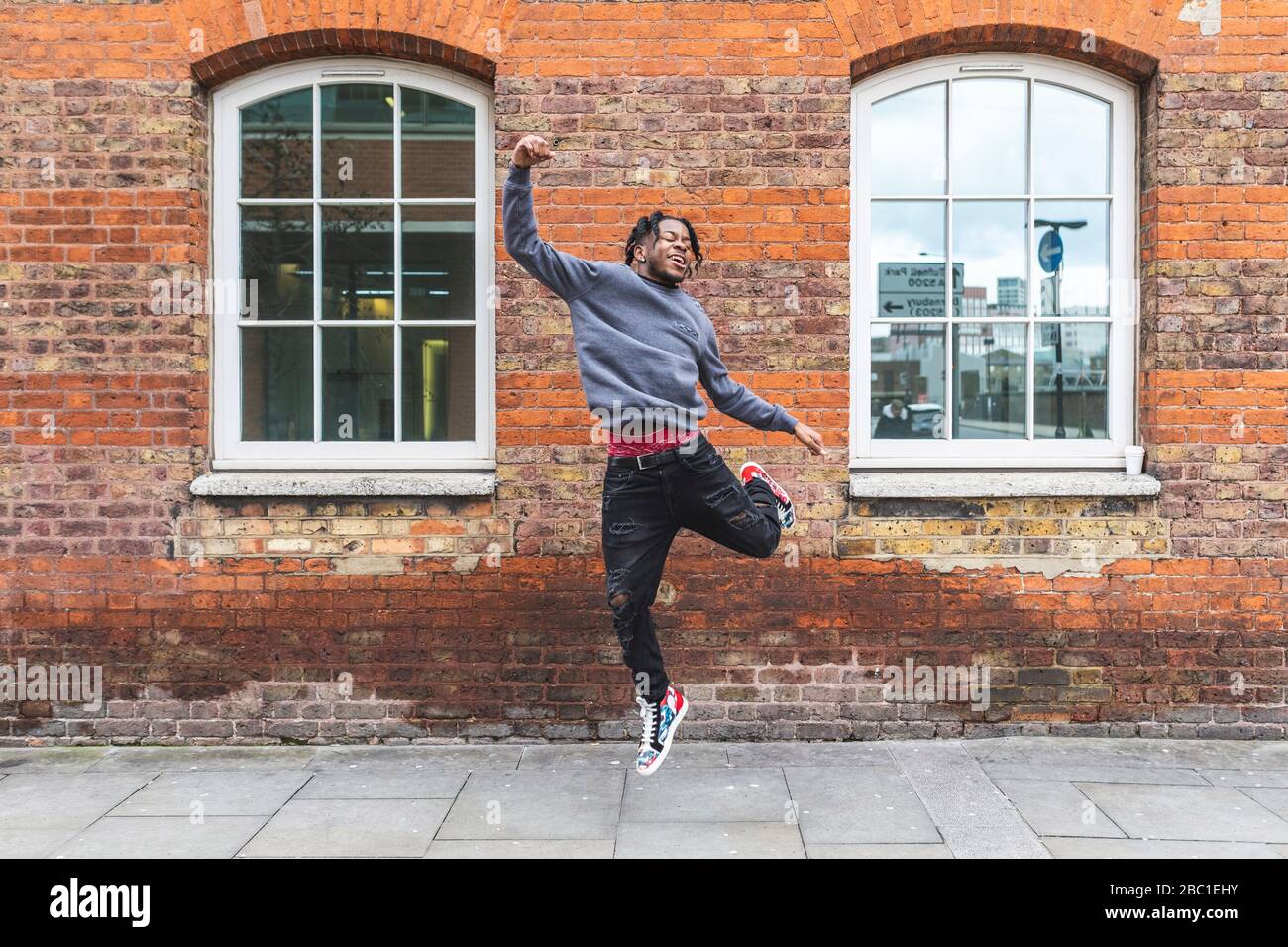 Young man jumping in front of brick wall Stock Photo - Alamy