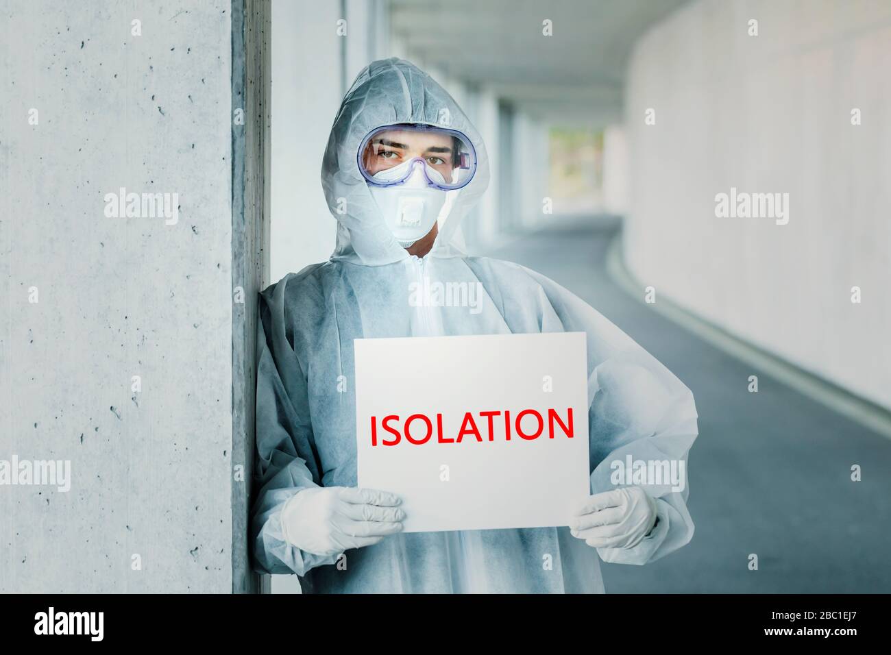 Portrait of man wearing protective clothing holding an 'isolation' sign ...