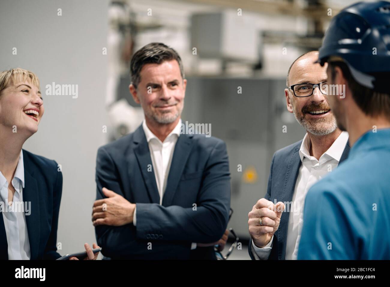 Happy business people looking at worker in a factory Stock Photo - Alamy