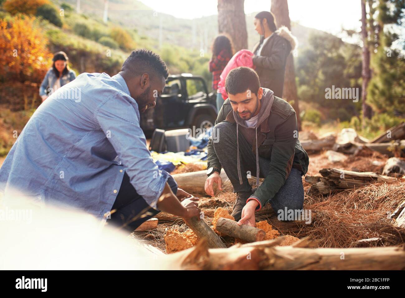 Young men friends building campfire at campsite Stock Photo - Alamy
