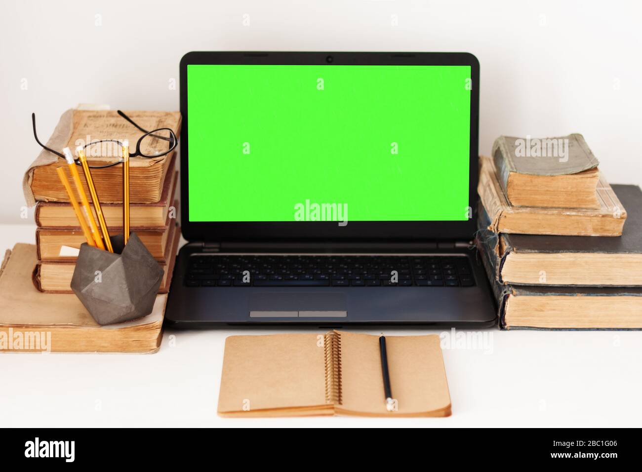 Home office: open textbook, notebook, green screen laptop computer ...