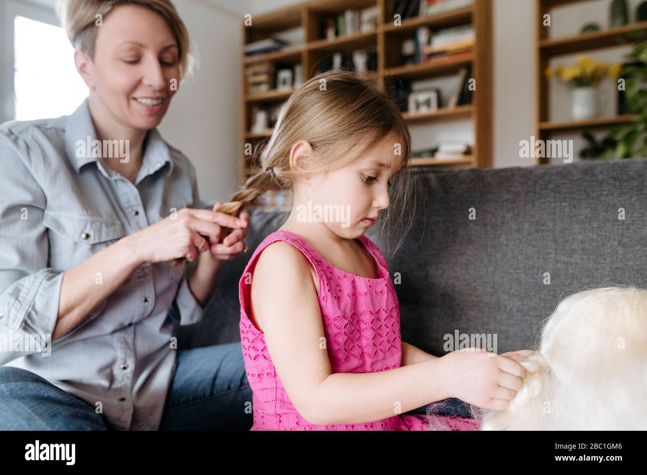 Mother braiding her daughter's hair on the couch Stock Photo - Alamy