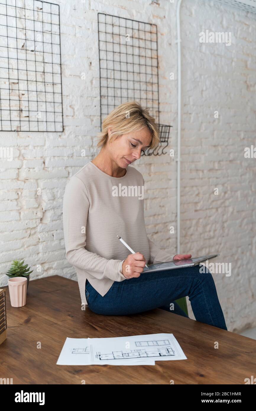 Mature woman at work sitting on desk in architectural office Stock ...