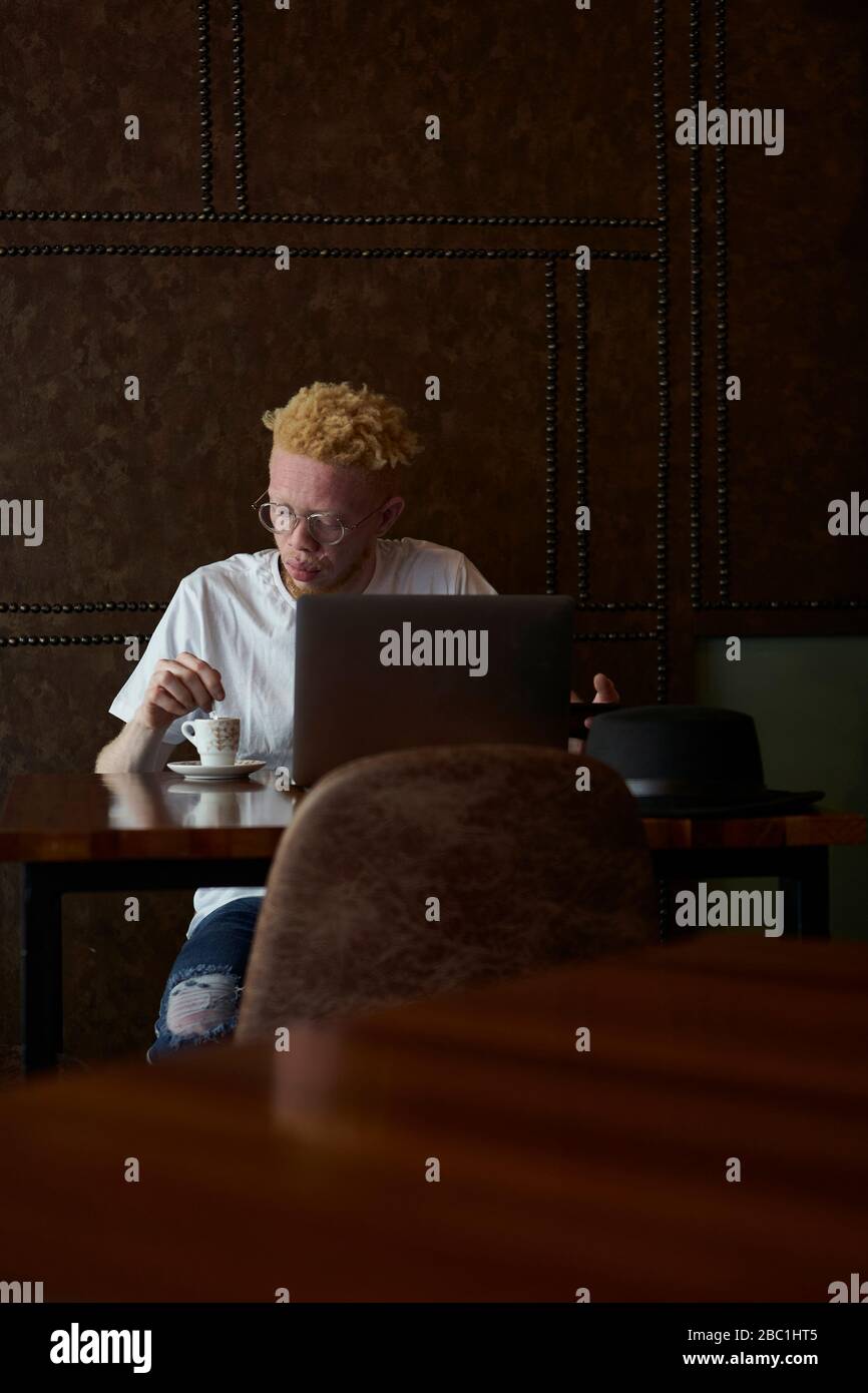 Albino man having a coffee and working on his computer in a cafeteria ...