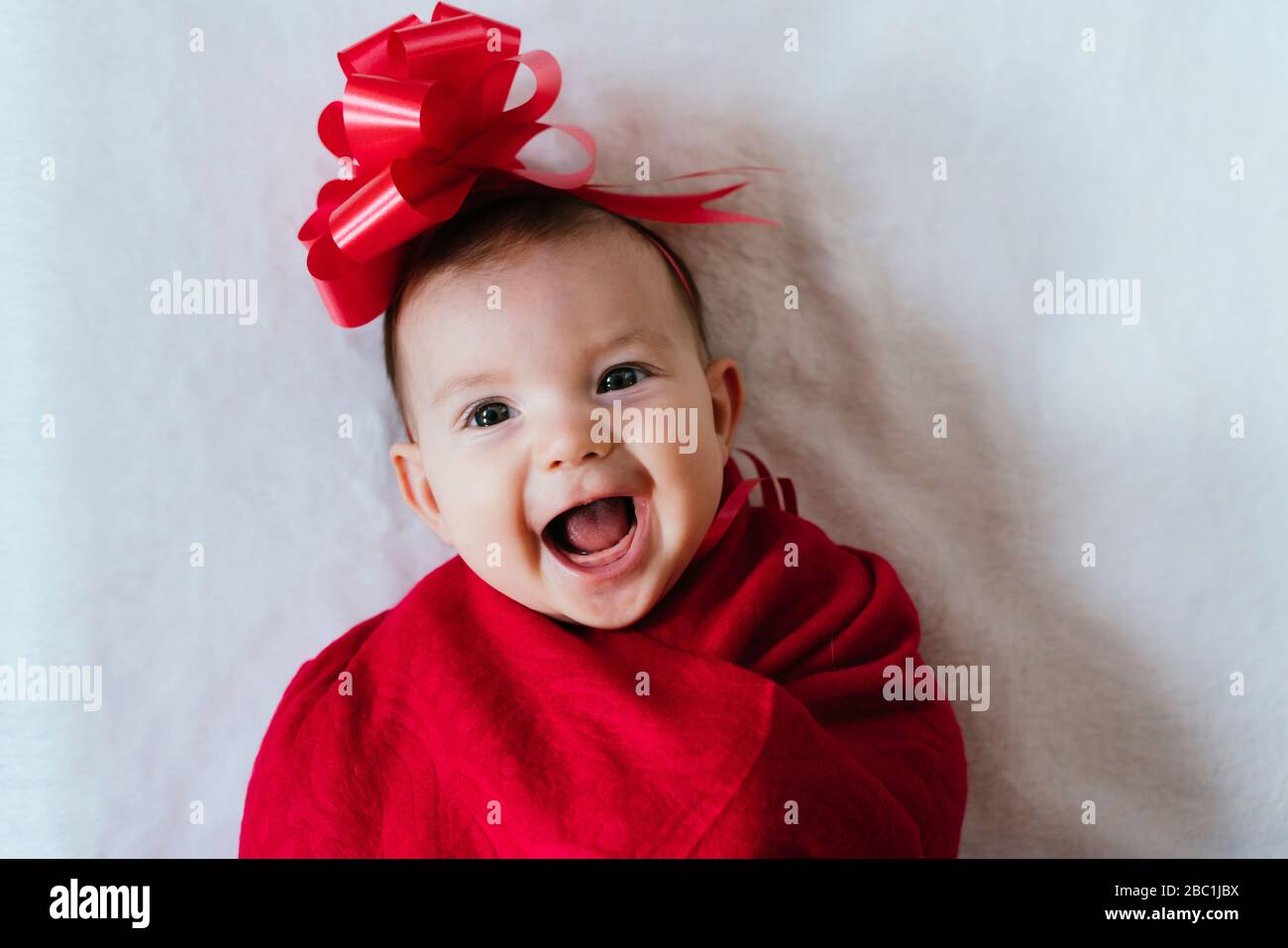 Portrait of happy baby girl with red ribbon on her head wrapped in red ...