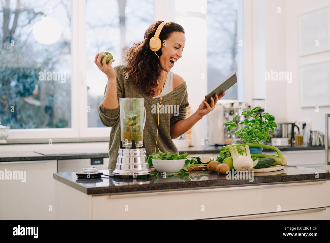 Fit woman standing in kitchen, preparing healthy smoothie, using online ...