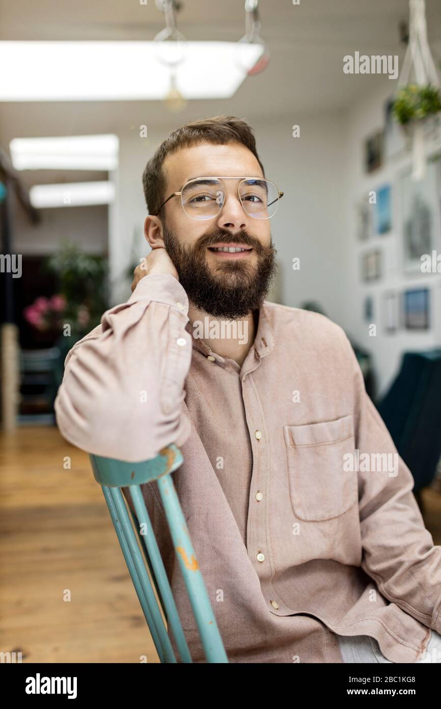 Young man sitting on chair, looking at camera, smiling Stock Photo - Alamy