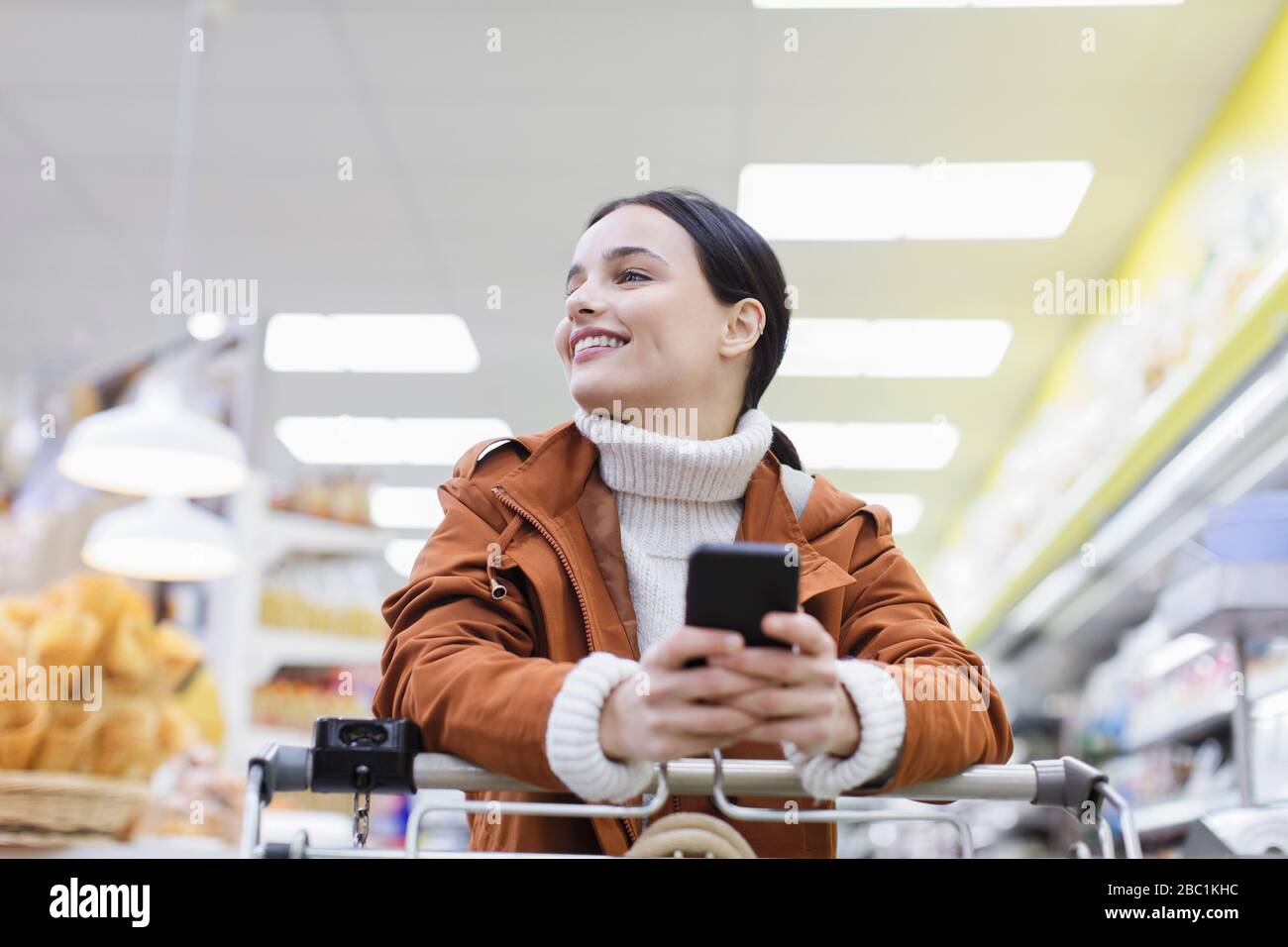 Smiling, confident woman with smart phone shopping in supermarket Stock ...