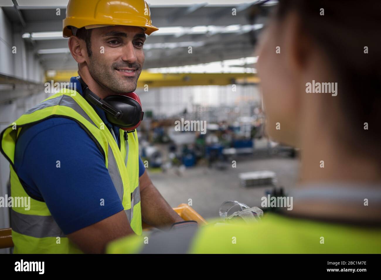 Smiling male supervisor talking to coworker on platform in factory ...
