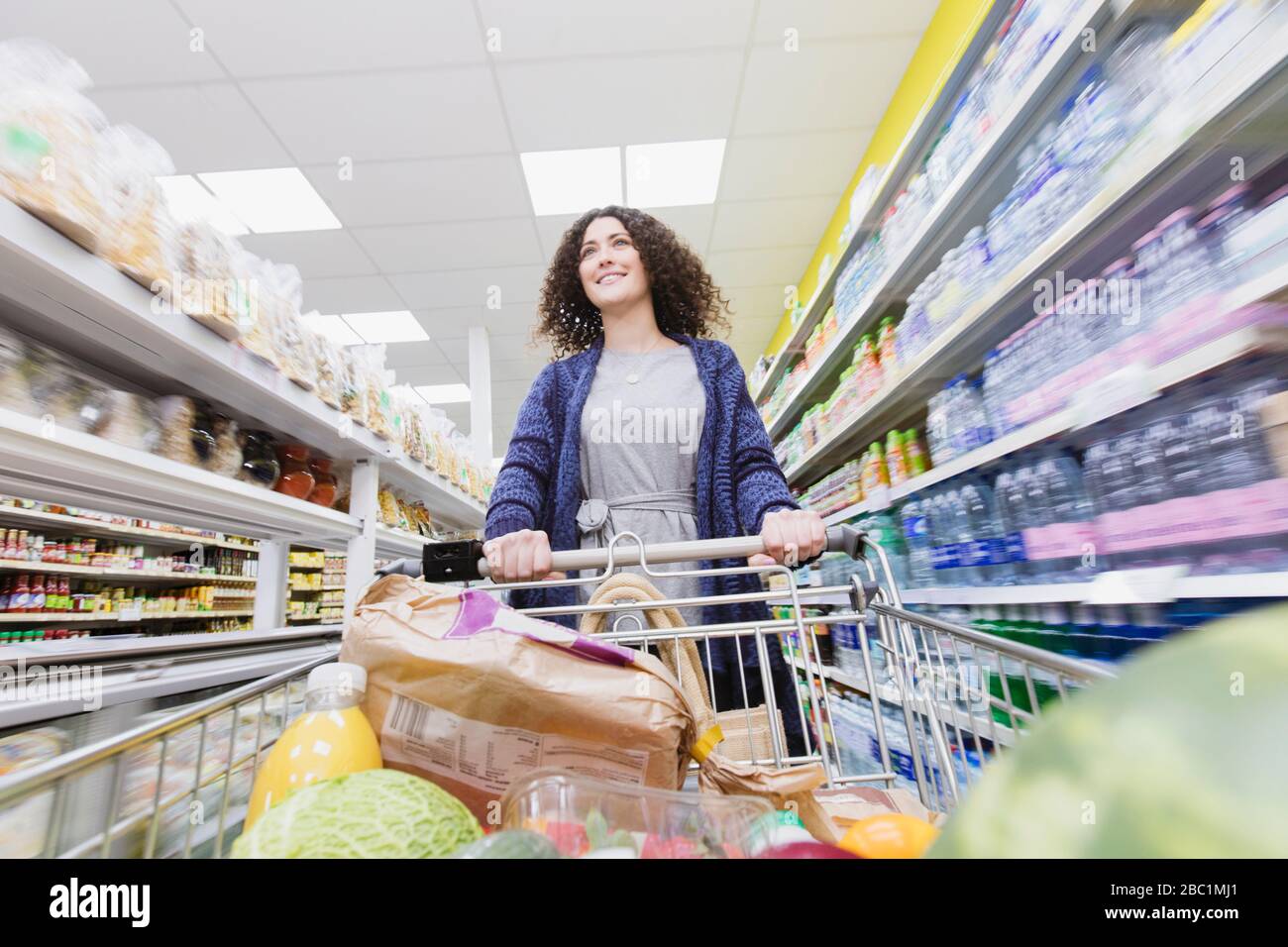 Woman pushing shopping cart in supermarket aisle Stock Photo - Alamy