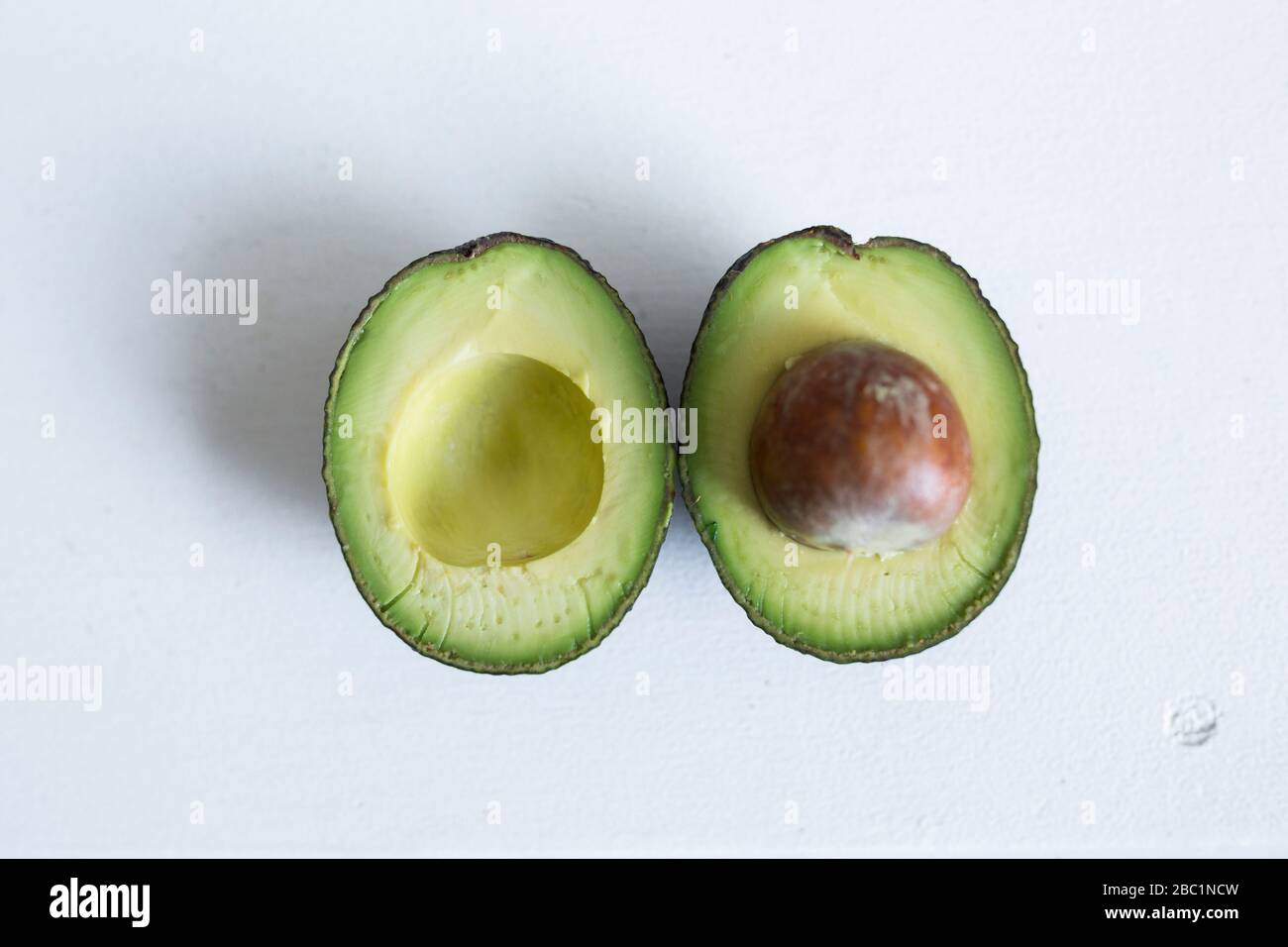 A sliced in half fresh, green avocado with the pit inside ready to be ...
