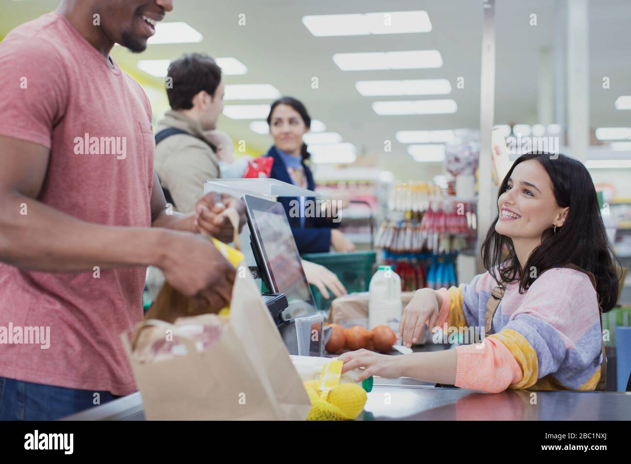 Friendly cashier helping customers at supermarket checkout Stock Photo ...