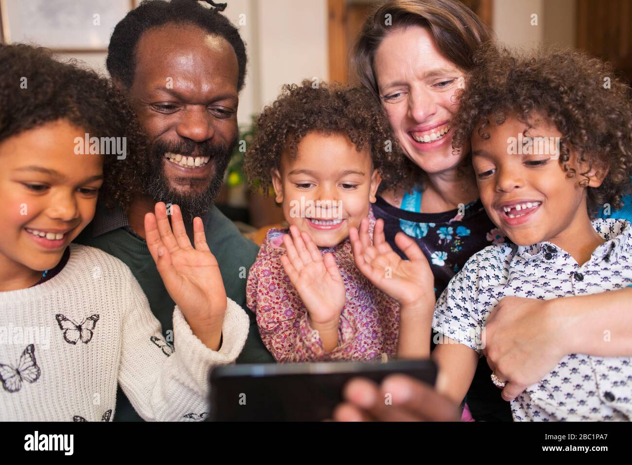 Happy multiethnic family waving and video chatting with smart phone ...
