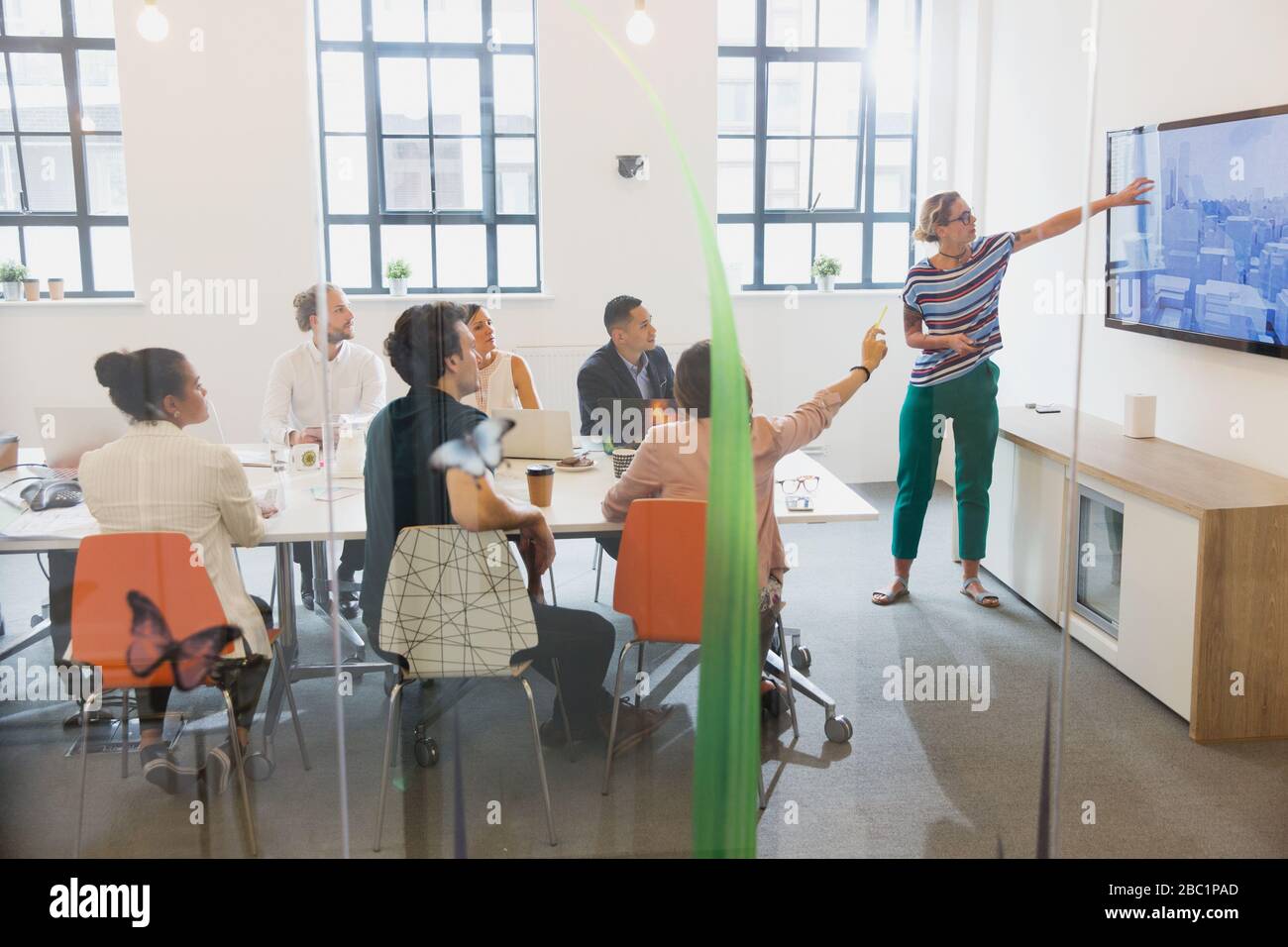 Female architect at television screen leading conference room meeting ...