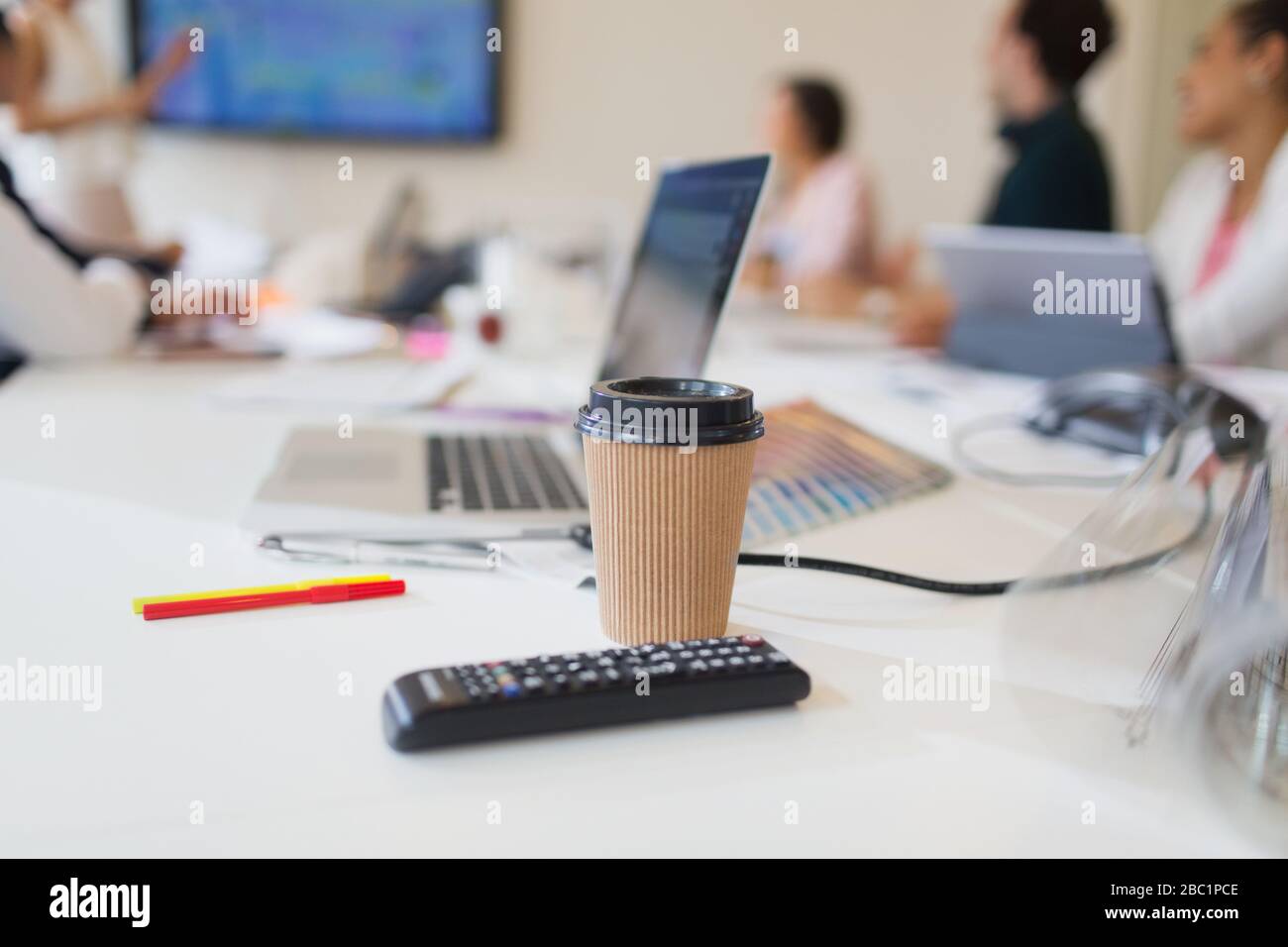 Disposable coffee cup and remote control on table in conference room ...