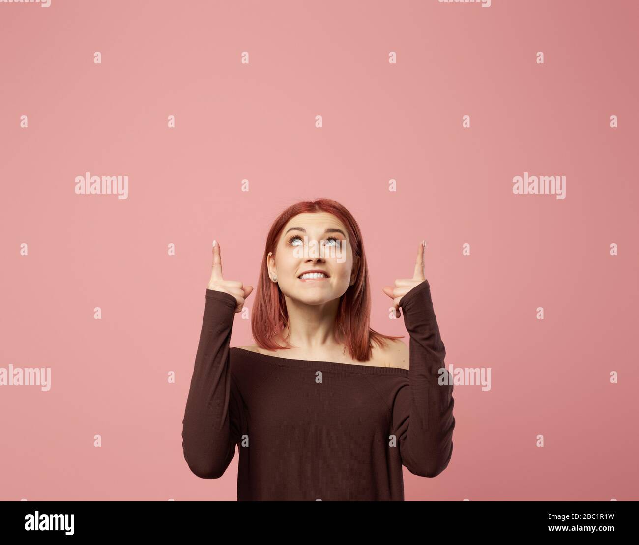 Happy girl with gray eyes pointing up isolated on empty pink background ...