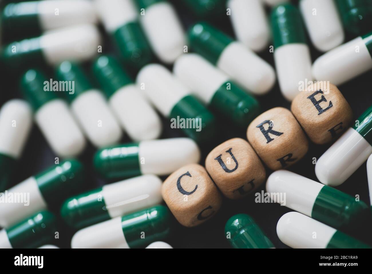 CURE word on wooden alphabet block with green pills as the background ...