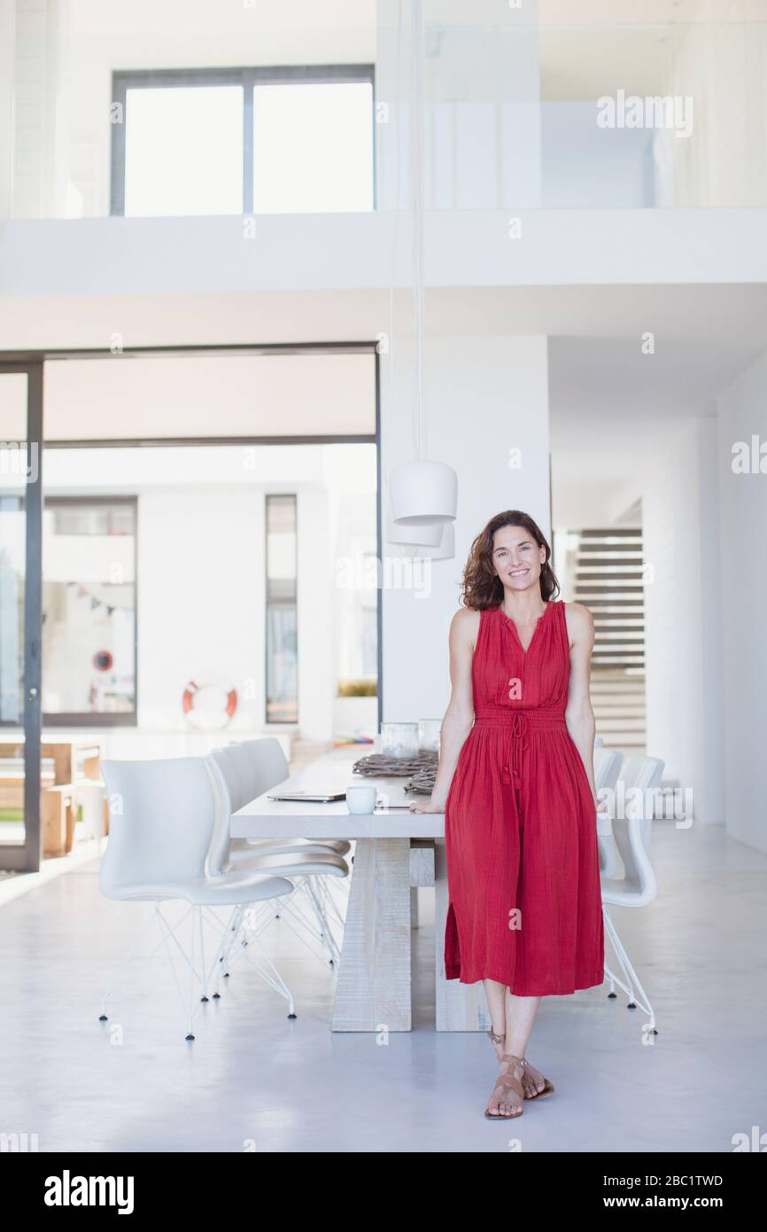 Portrait smiling brunette woman in red dress leaning on dining table ...