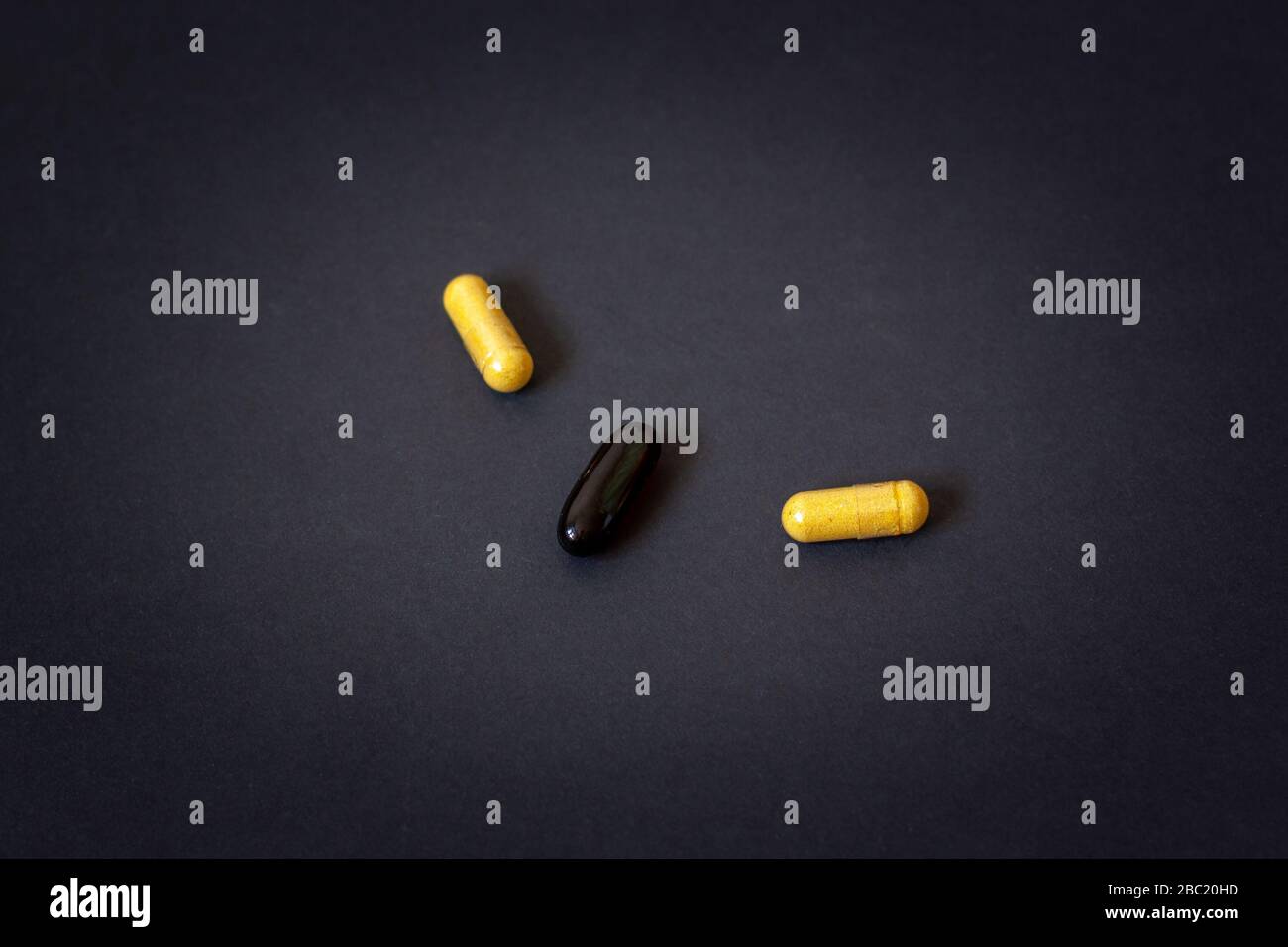 Three pills in capsules on a dark background. Yellow and black tablets ...