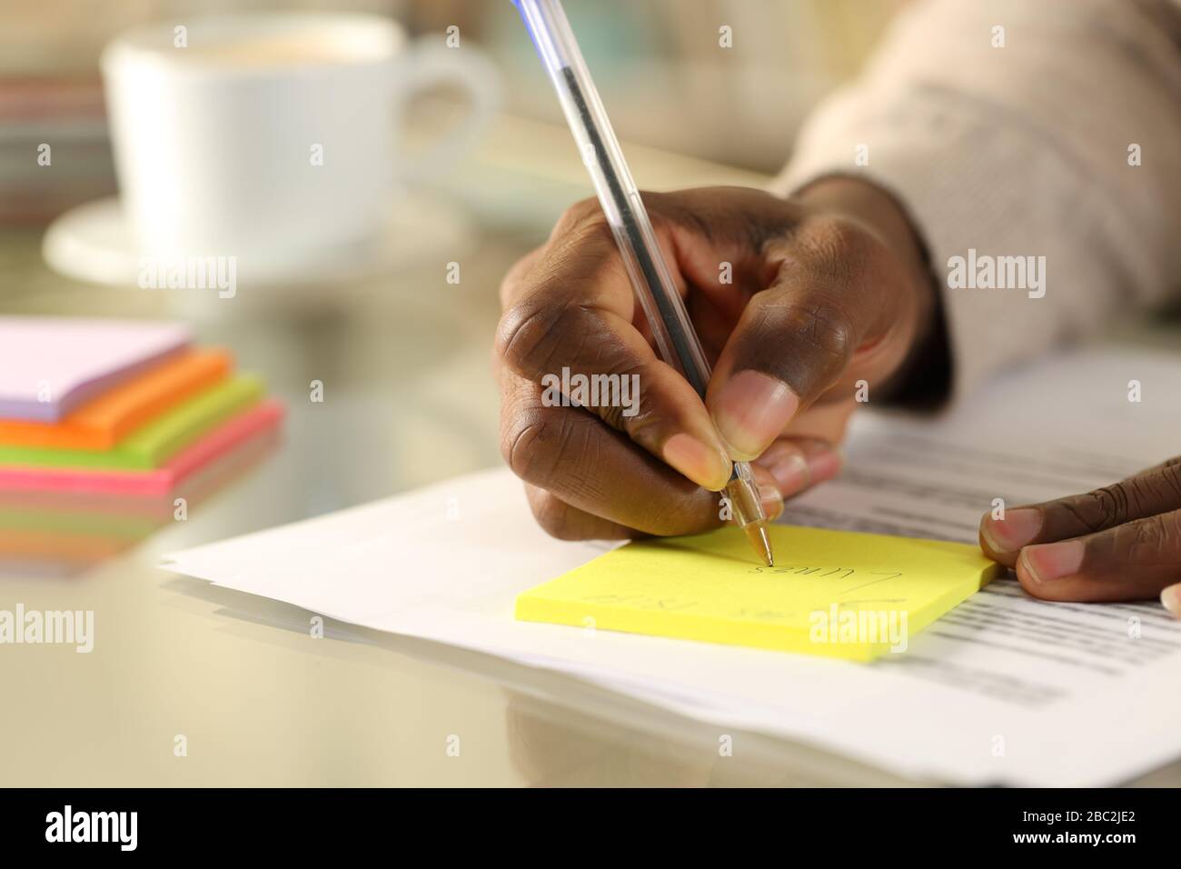Close up of black man hand writing reminder on sticky note on a desk at ...