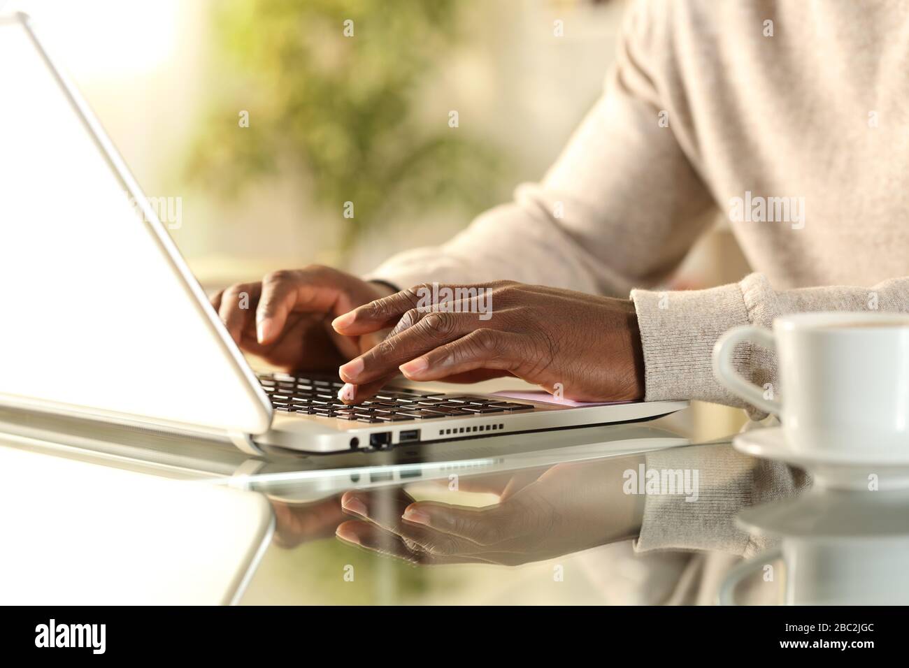 Close up of black man hands typing on a laptop sitting on a desk at ...