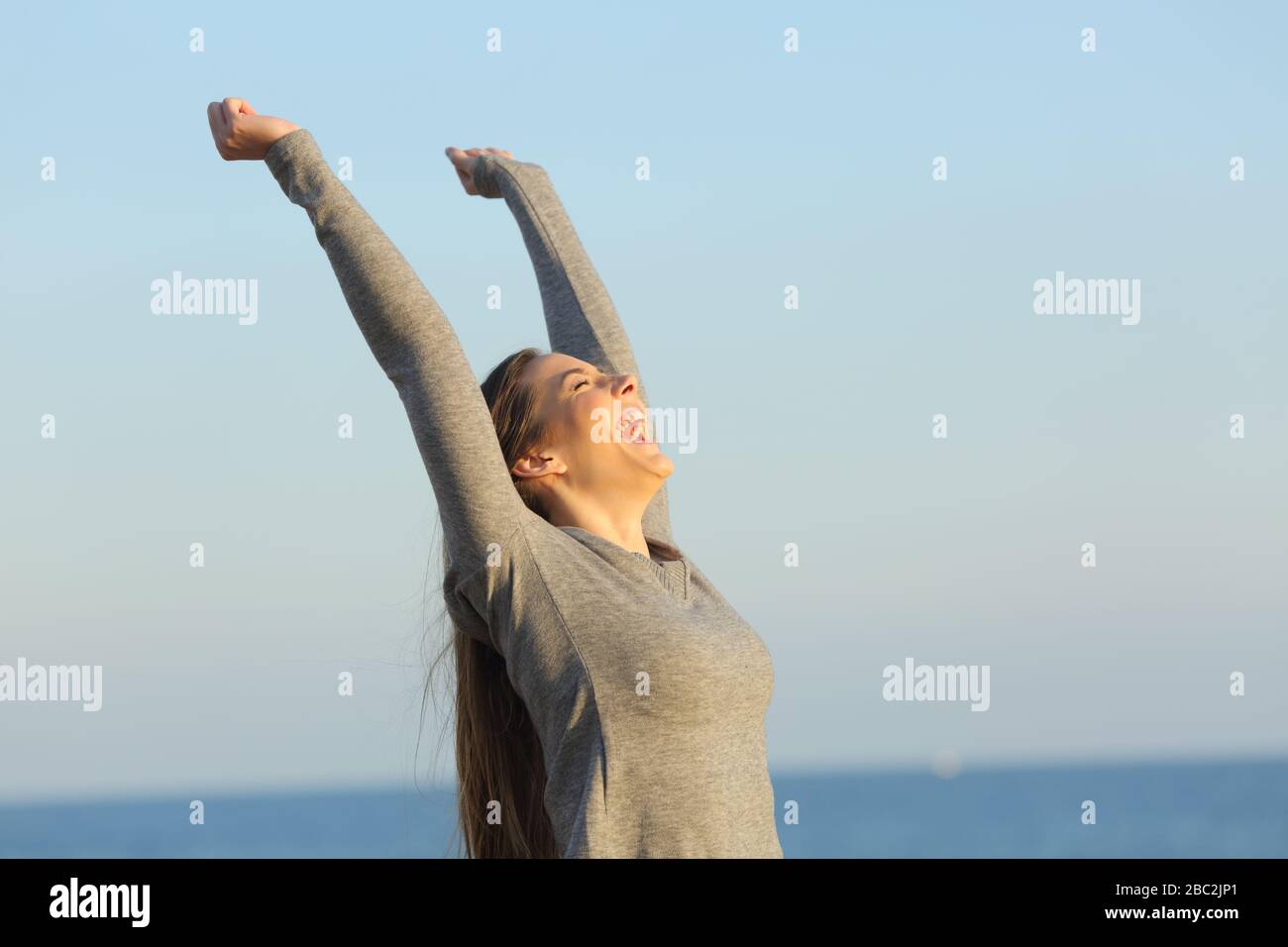Excited woman celebrating success raising arms on the beach at sunset ...