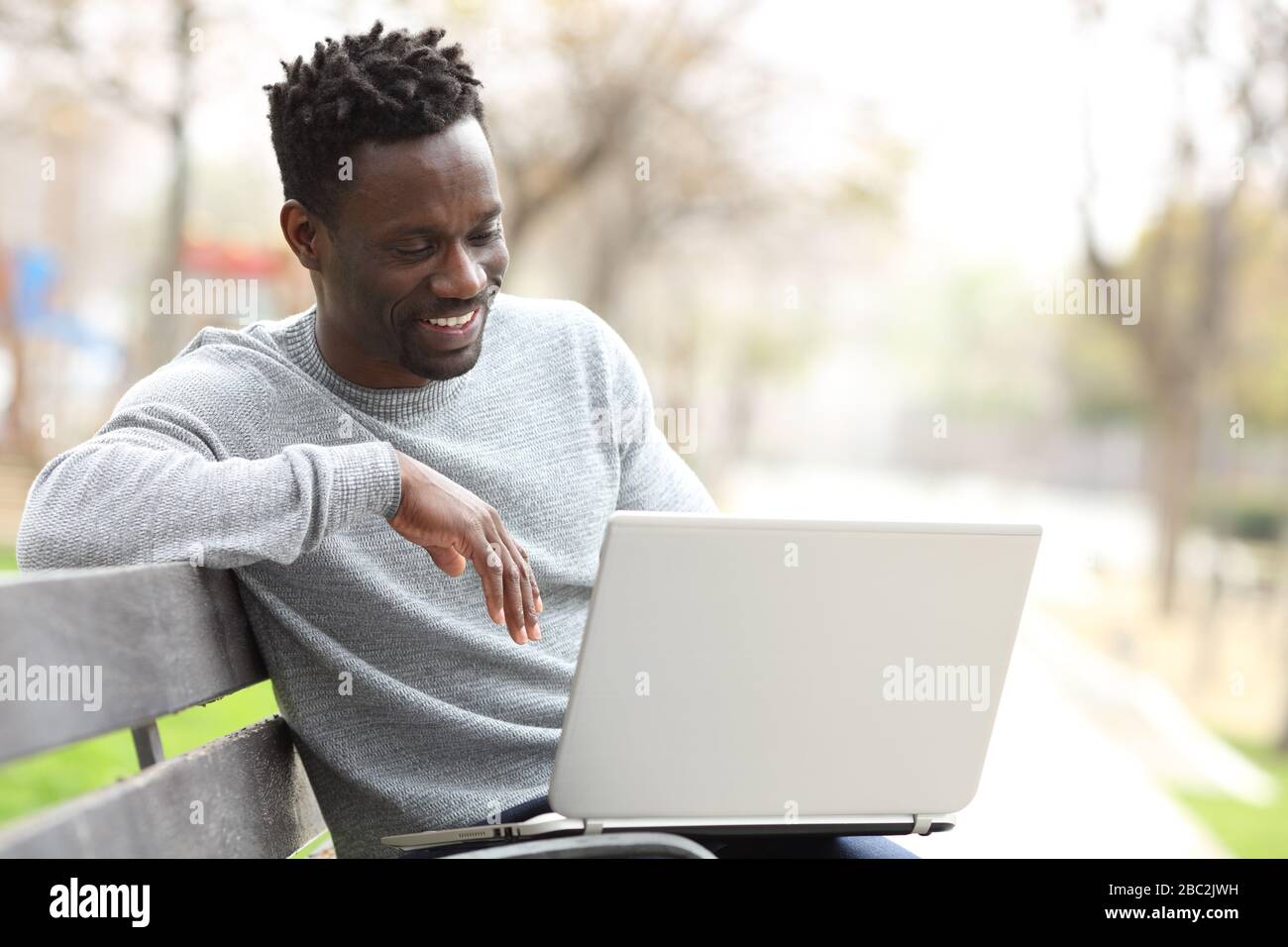 Happy black man using a laptop sitting on a bench in a park Stock Photo ...
