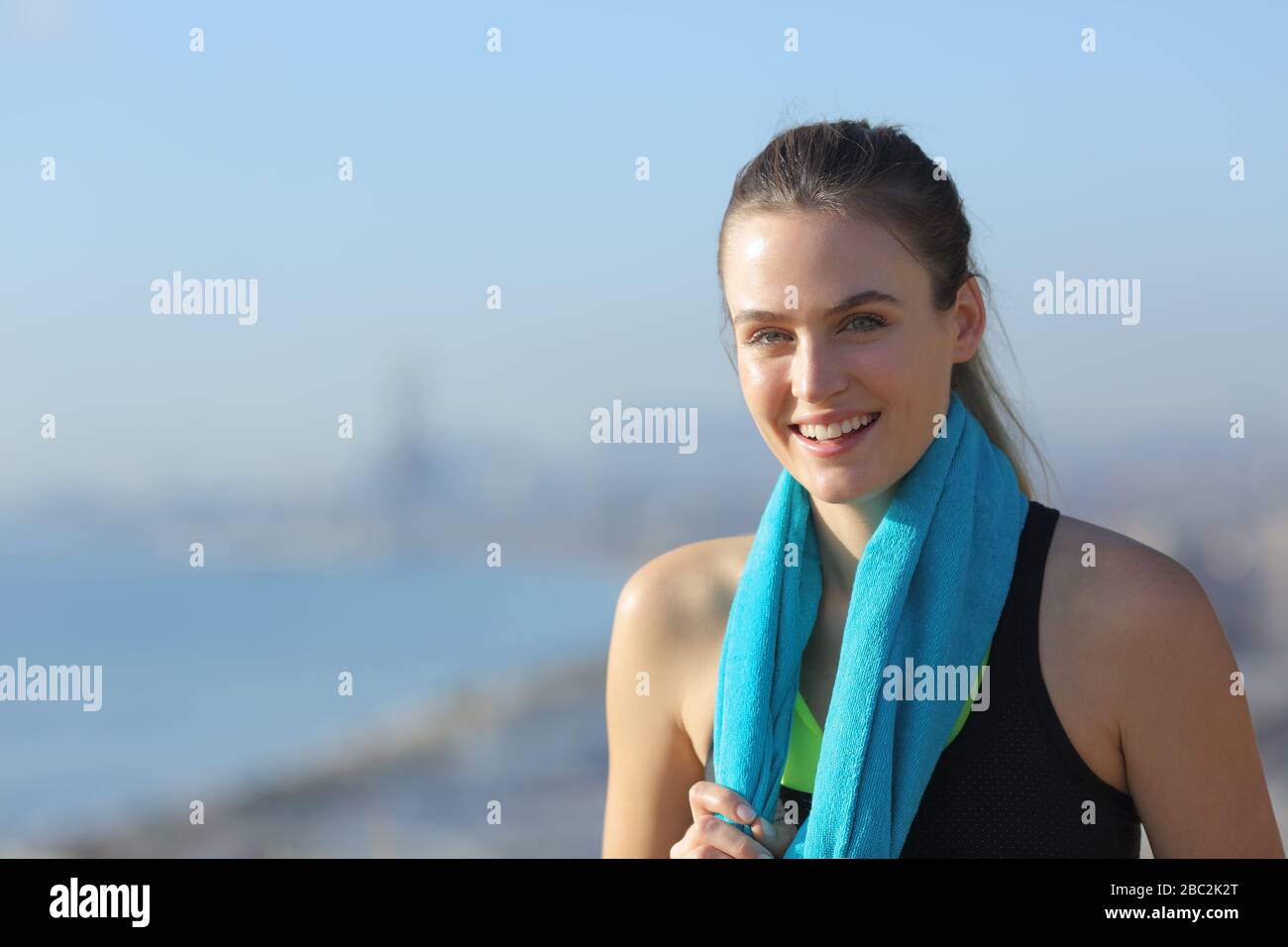 Portrait of a happy runner woman looking at camera wearing a towel on ...