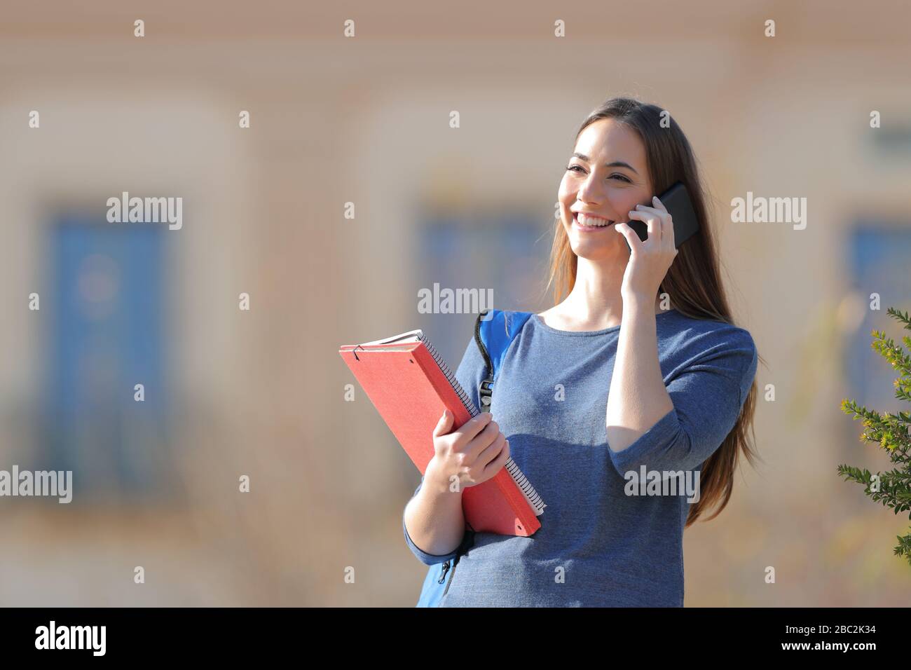 Happy student talks on mobile phone standing in an university campus ...