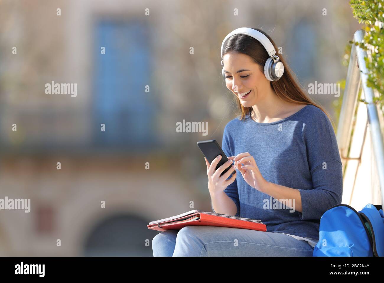 Happy student listening to music sitting outdoors in a university ...