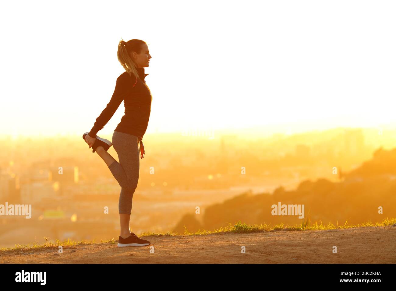 Full body profile of a runner woman stretching leg alone in city ...