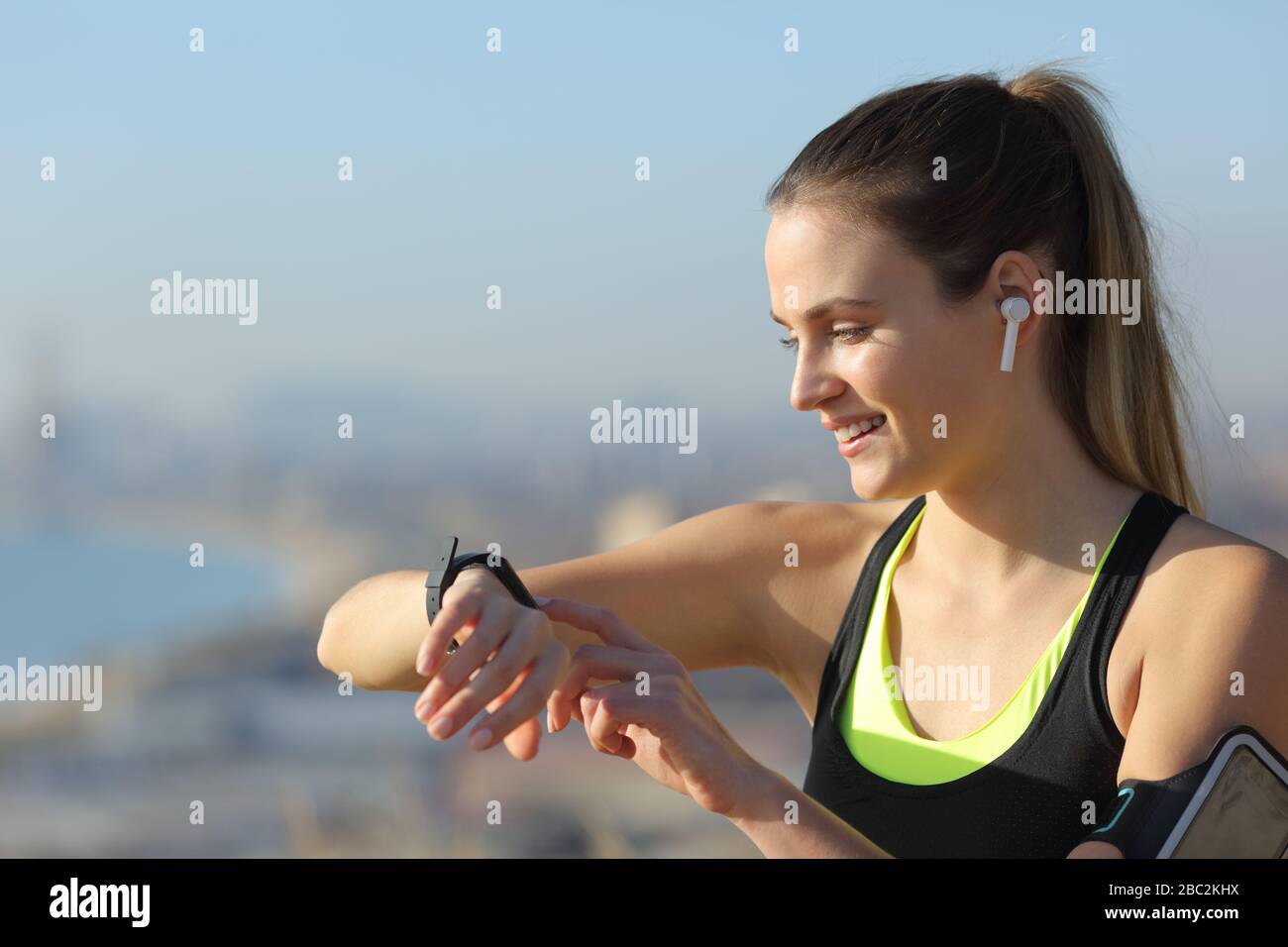 Runner wearing earbuds checks music on smartwatch outdoors in a city ...