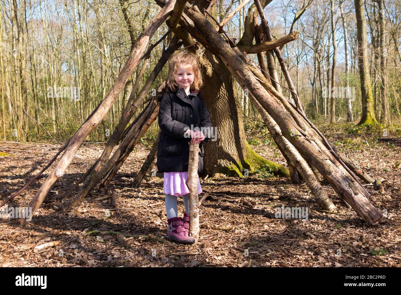Young girl / kids / kid / and a wigwam stack of trees branches leant up ...