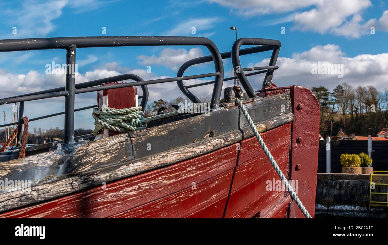 The front end of a red ship. old red wooden ship. rope is tied to ship ...
