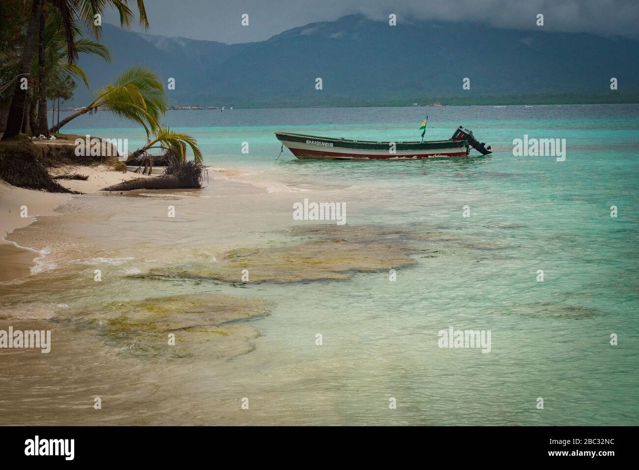 A small motorized fishing boat anchors on the beach of an island in the ...