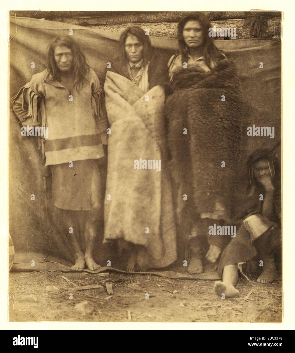 Group of Native Americans, three standing, one seated on the ground ...