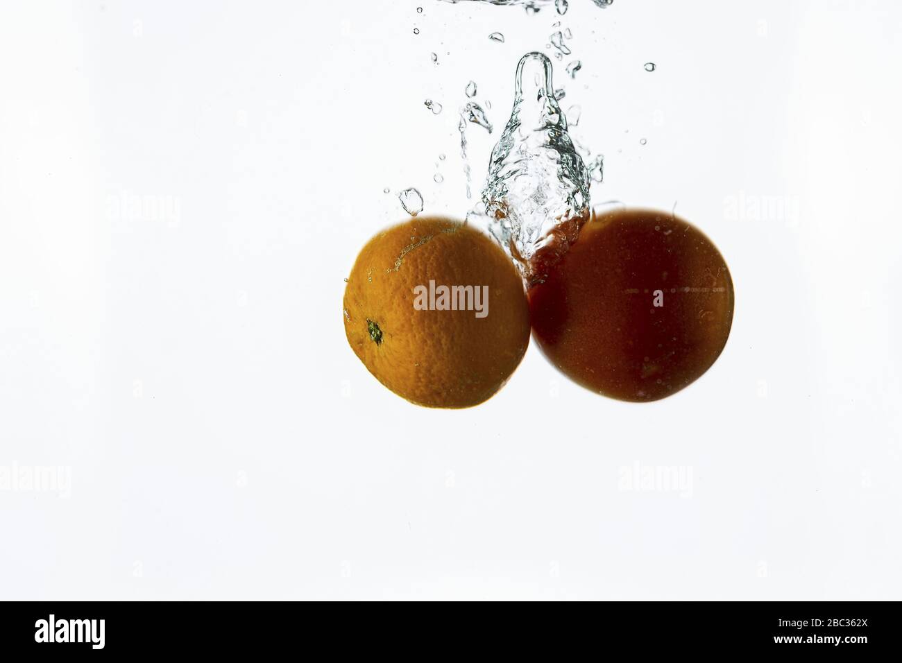 Close up view splashing water and red tomato and mandarin on white ...