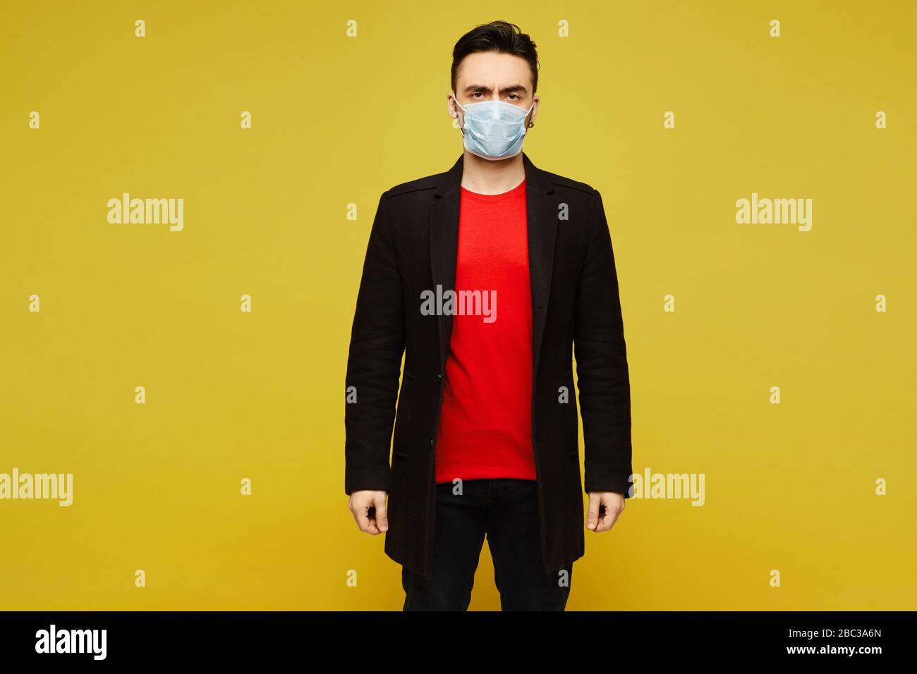 Young angry man in a red t-shirt and coat wears a protective medical ...
