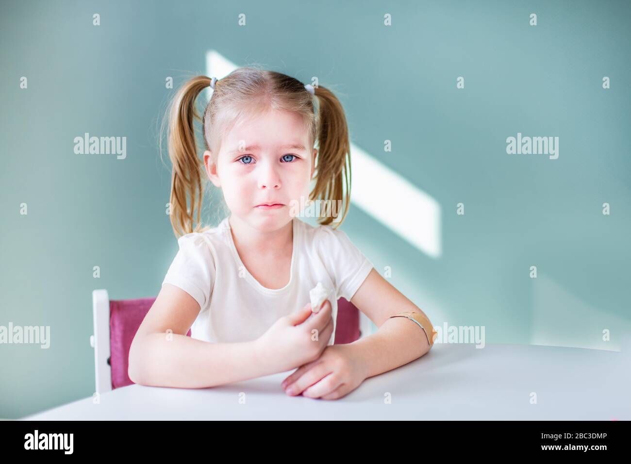 Little blonde girl with two ponytales is crying sitting by the white ...