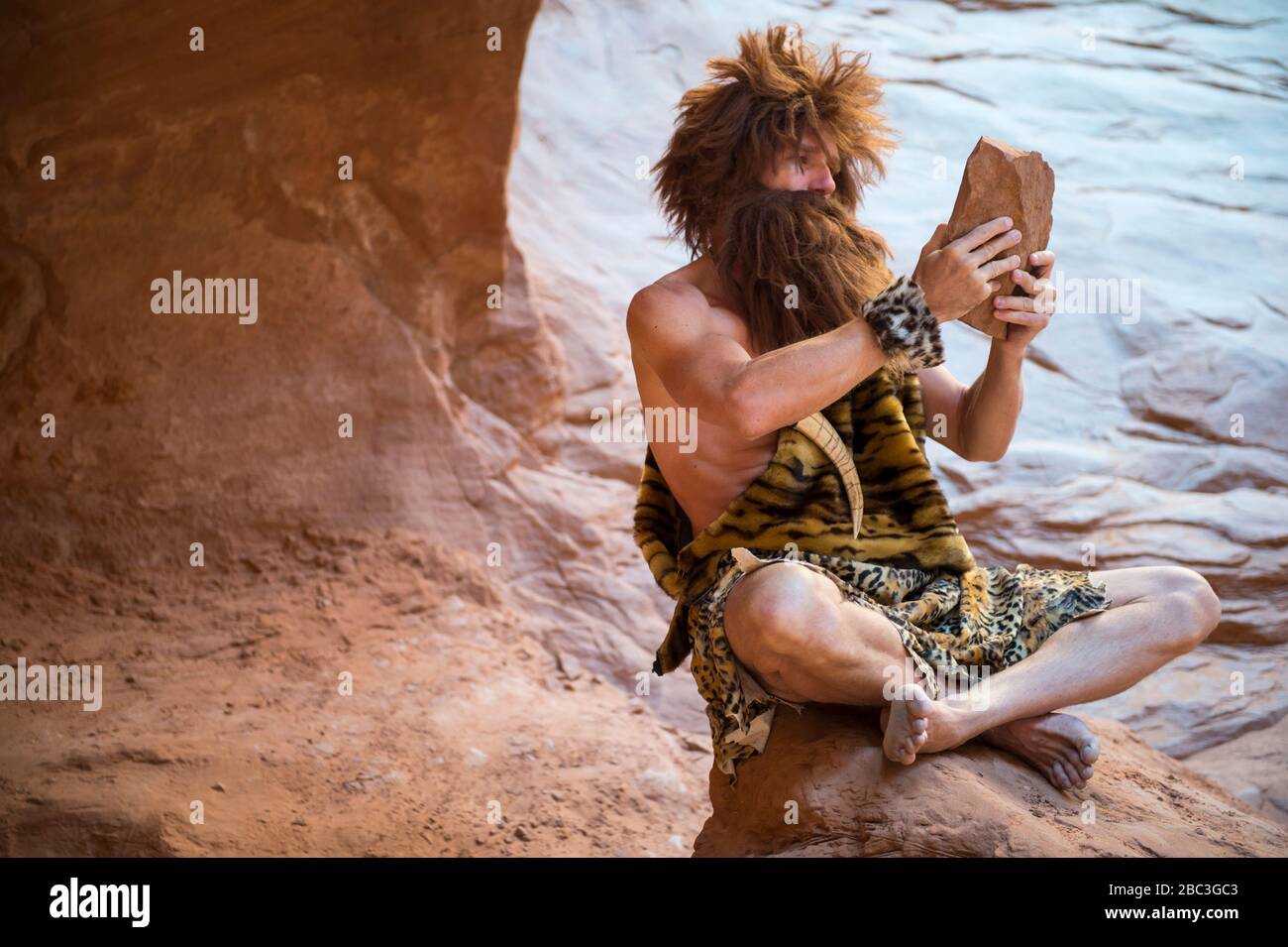 Caveman watching the screen of his primitive stone tablet outdoors in a ...