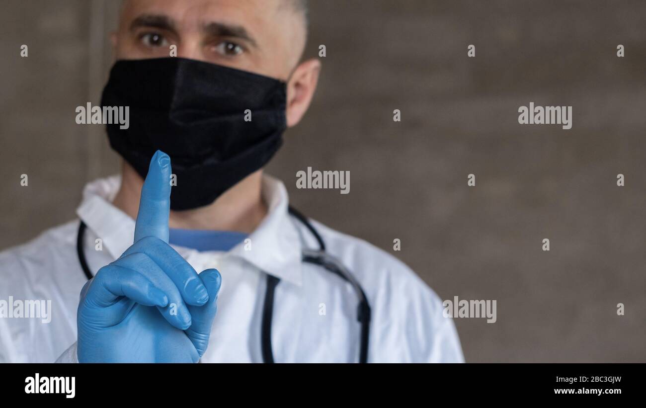 Male doctor in black protective mask and blue gloves shows forefinger ...